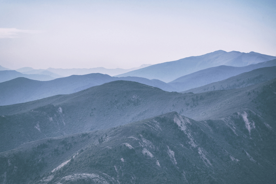 Distant mountain range under a soft hazy blue sky with layered hills ...
